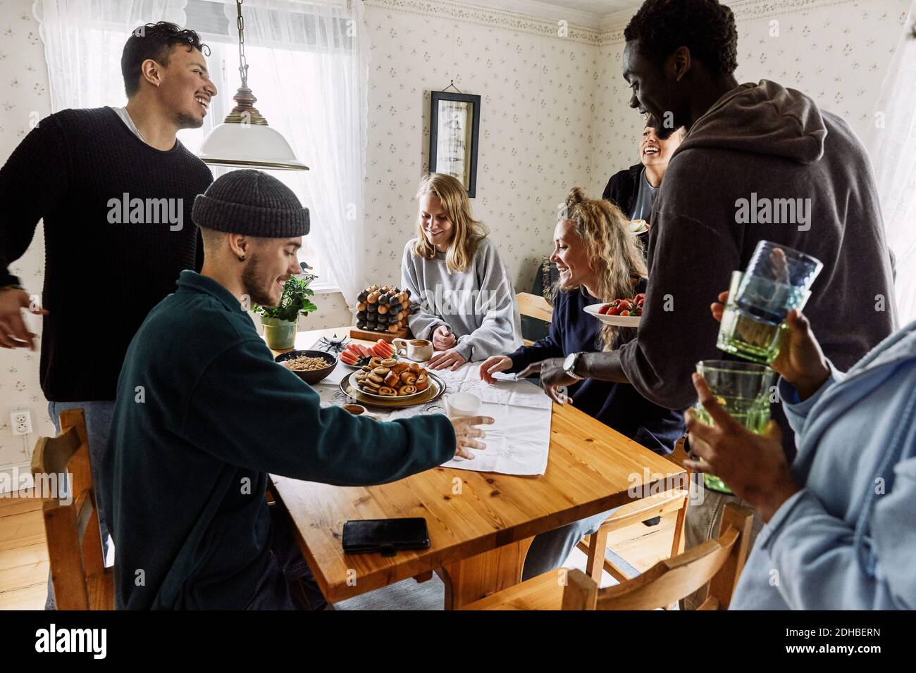 Happy friends placing food and drink on wooden table at home Stock ...