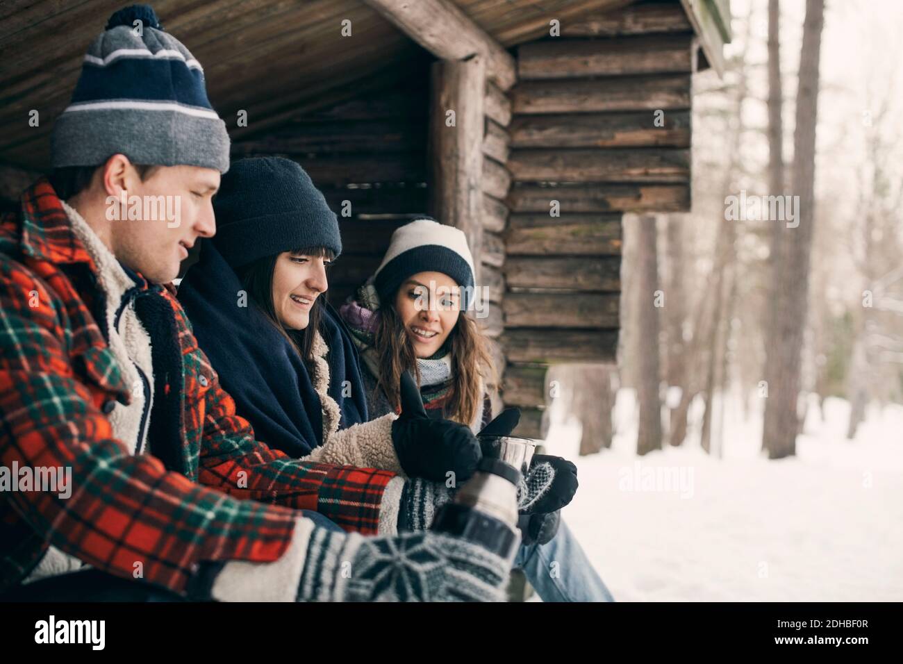 Man giving drink to female friends while sitting at log cabin during ...