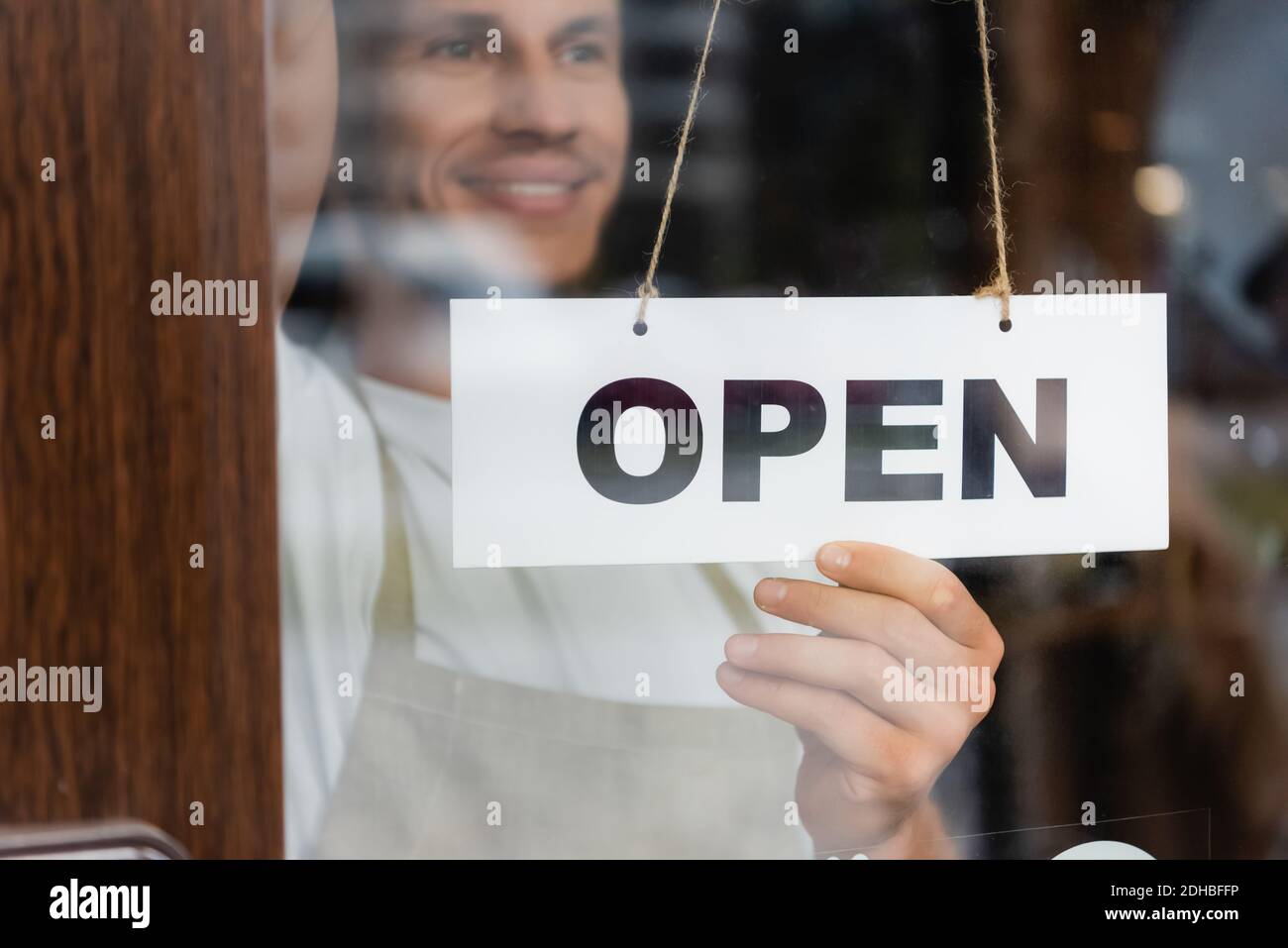 smiling barista hanging card with open lettering on door of cafe ...