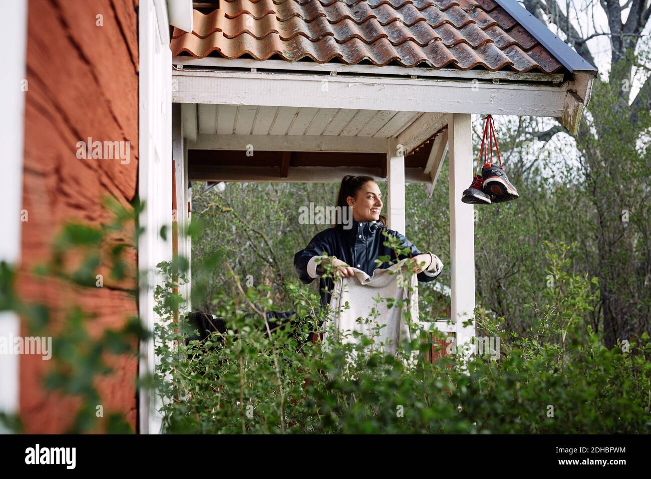 Smiling young woman drying clothes while standing outside cottage Stock ...