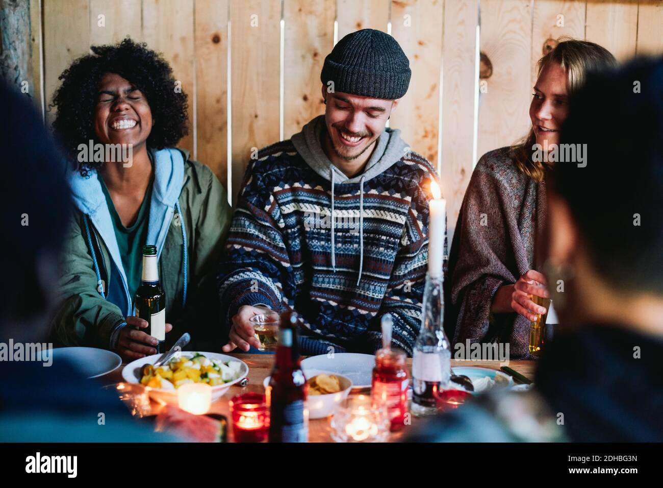 Cheerful friends holding drinks talking while sitting in log cabin ...