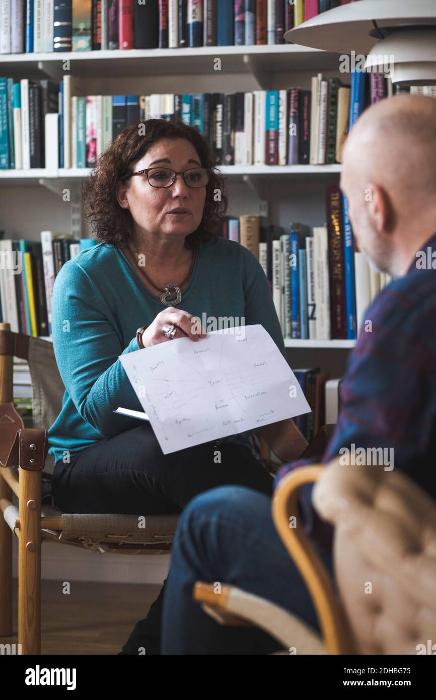 Mature female therapist showing analysis to patient against bookshelf ...