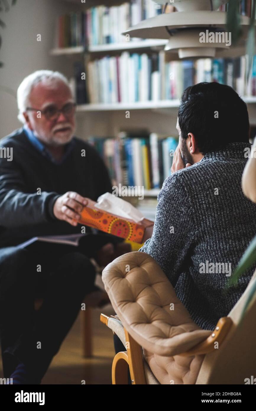Therapist giving tissue box to male patient at home office Stock Photo ...