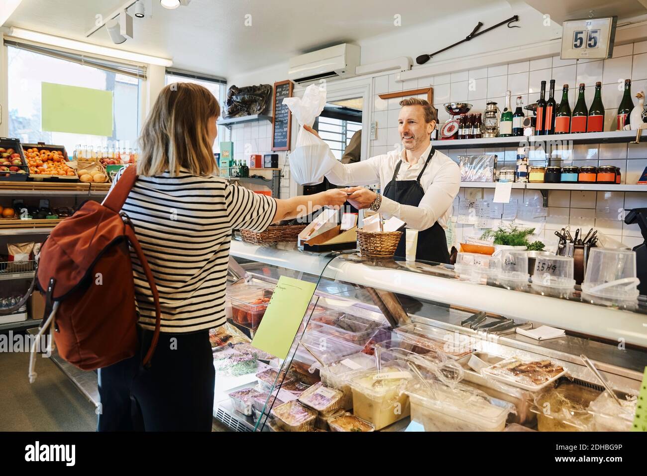 Male sales clerk holding plastic bag while accepting credit card from ...