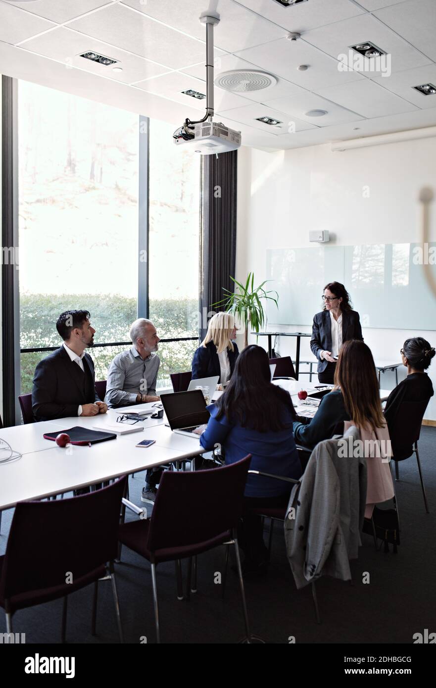 Businesswoman interacting to female colleague sitting with coworkers at ...