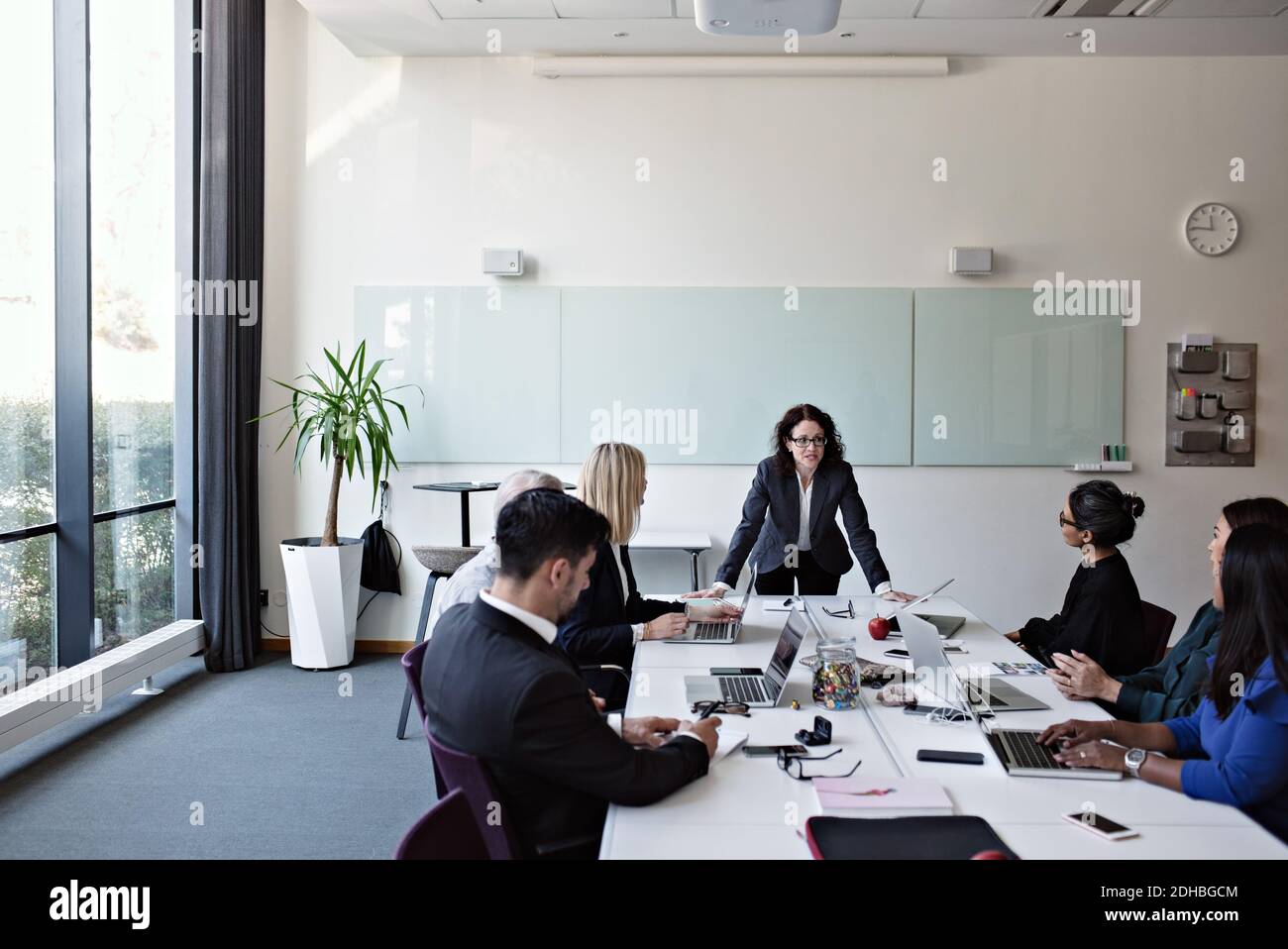 Businesswoman interacting with colleagues sitting at conference table ...