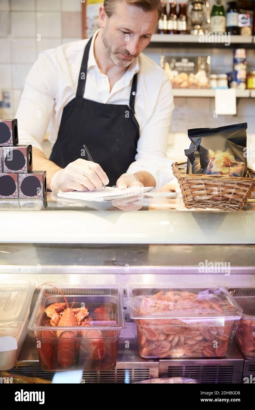 Male owner writing in note pad while standing at counter in store Stock ...