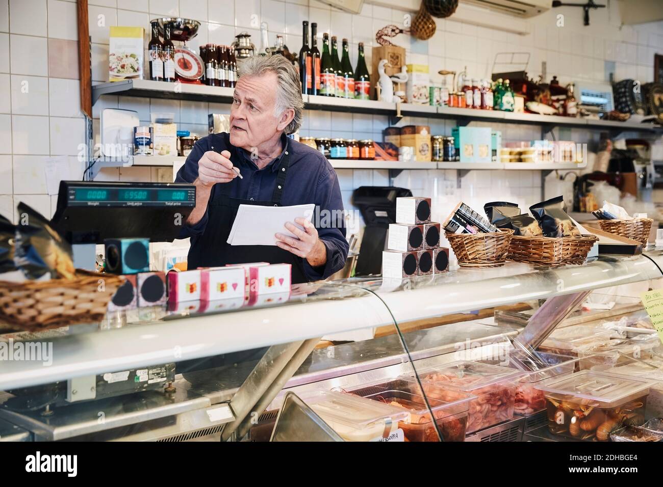 Male owner looking away while holding pen and note pad at counter in ...