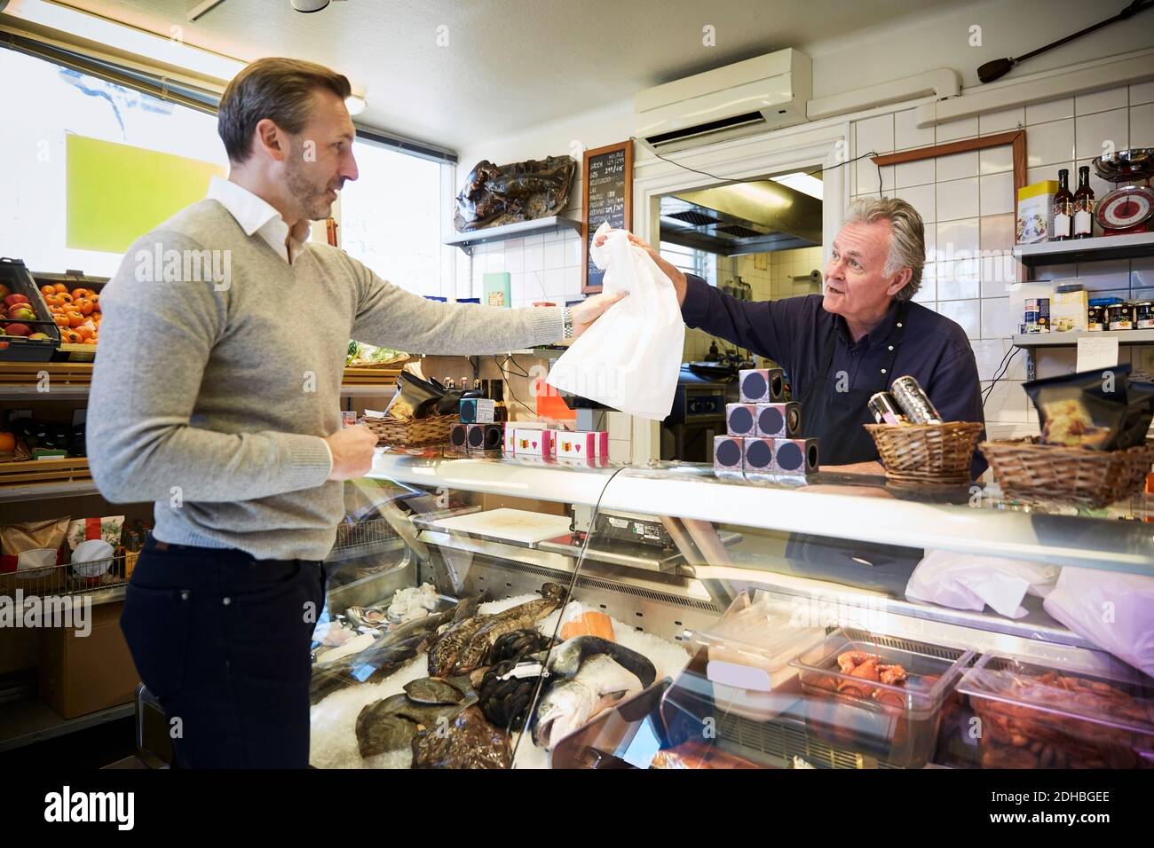 Male sales clerk handing over bag to customer at counter in store Stock ...