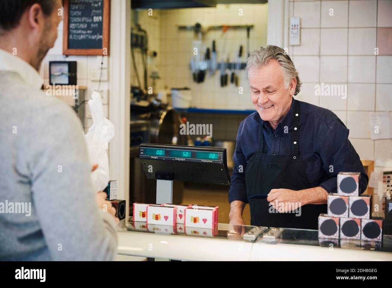 Smiling male sales clerk looking at weight scale while customer ...