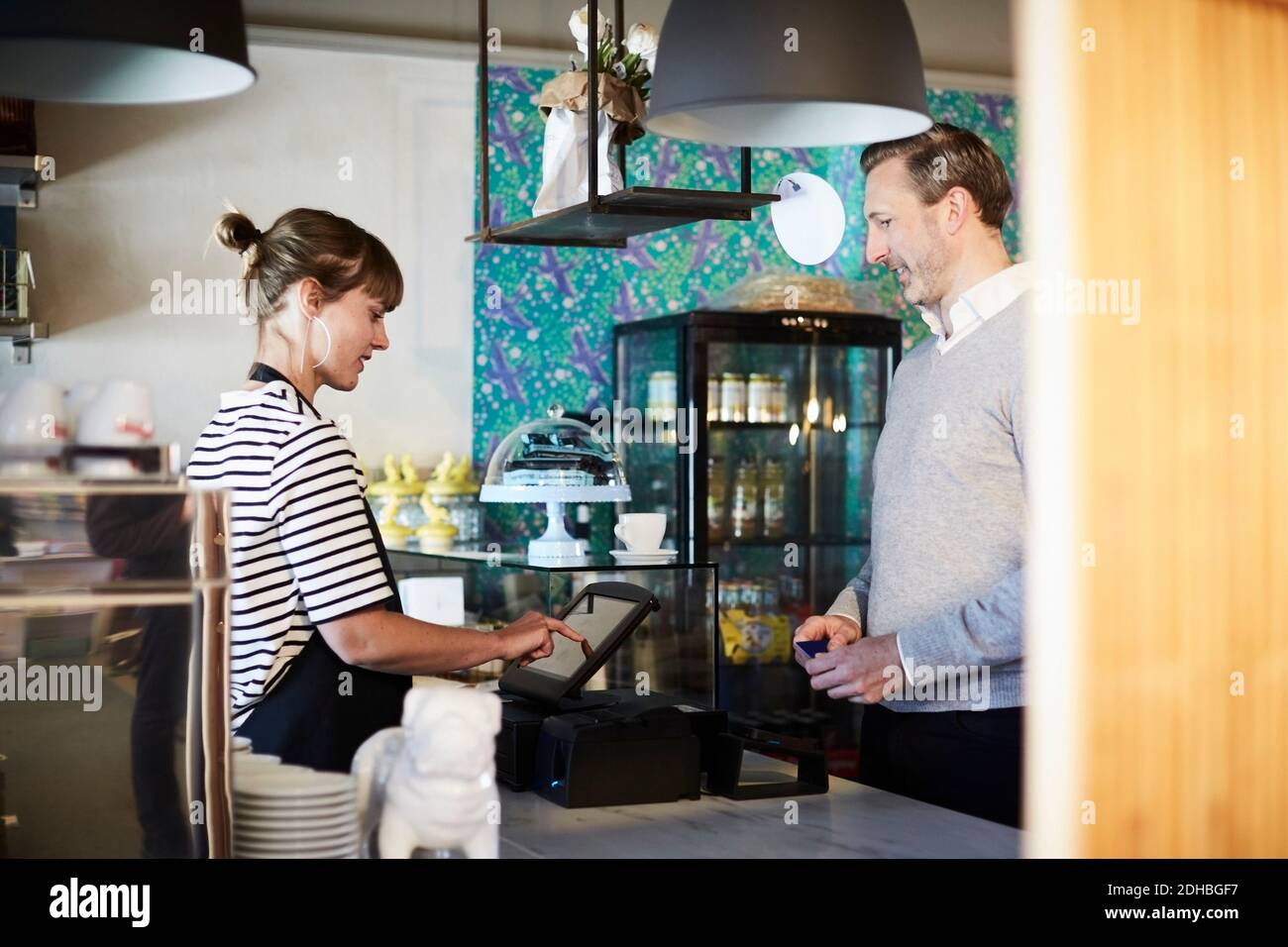 Male customer looking at female barista using cash register in cafe ...