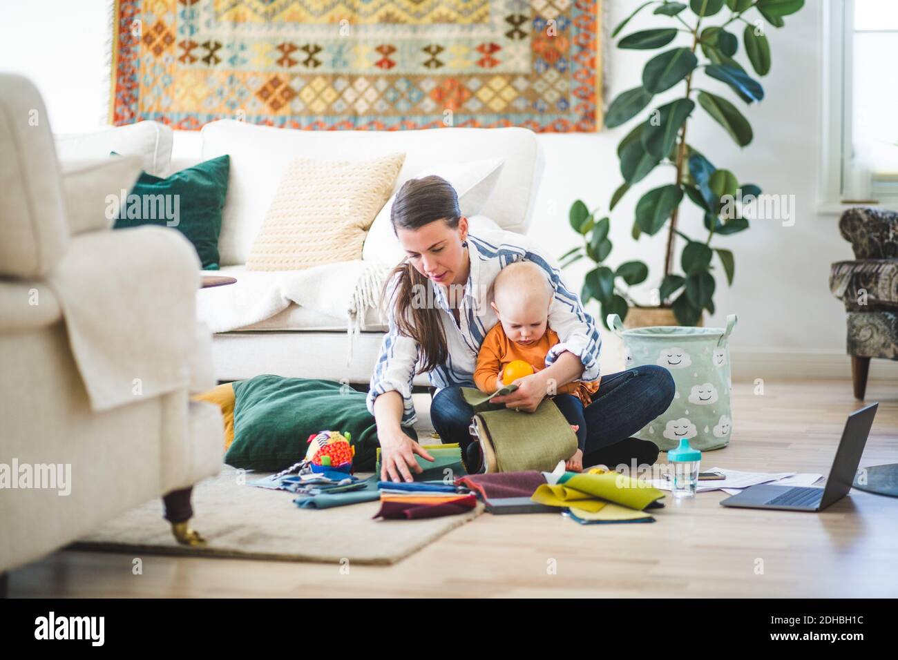 Full length of multi-tasking mother with fabric swatches and daughter ...