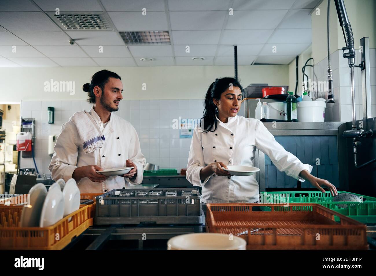 Male and female chefs communicating while holding plates in kitchen ...