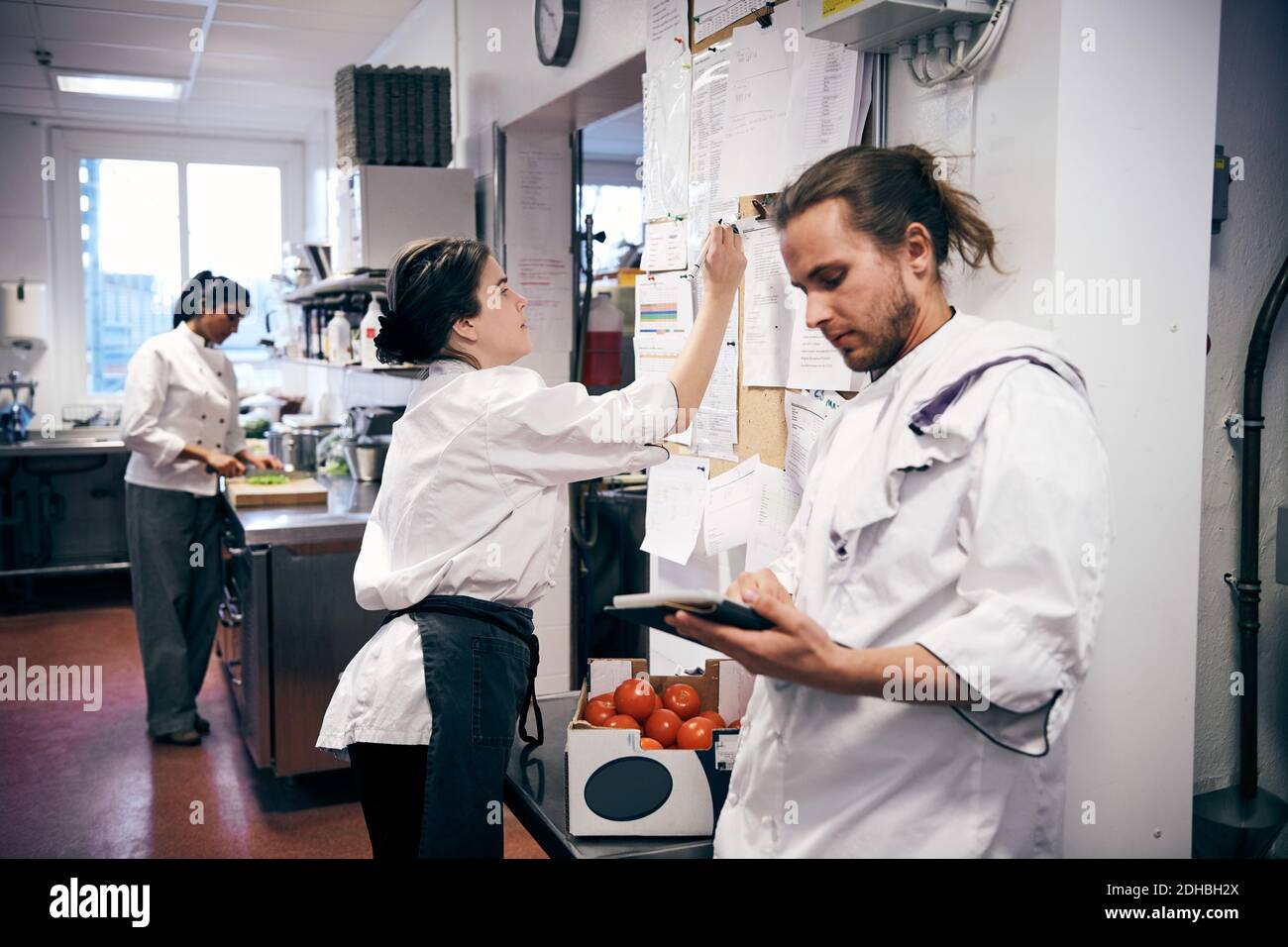 Female chef making checklist while colleagues working in kitchen Stock ...