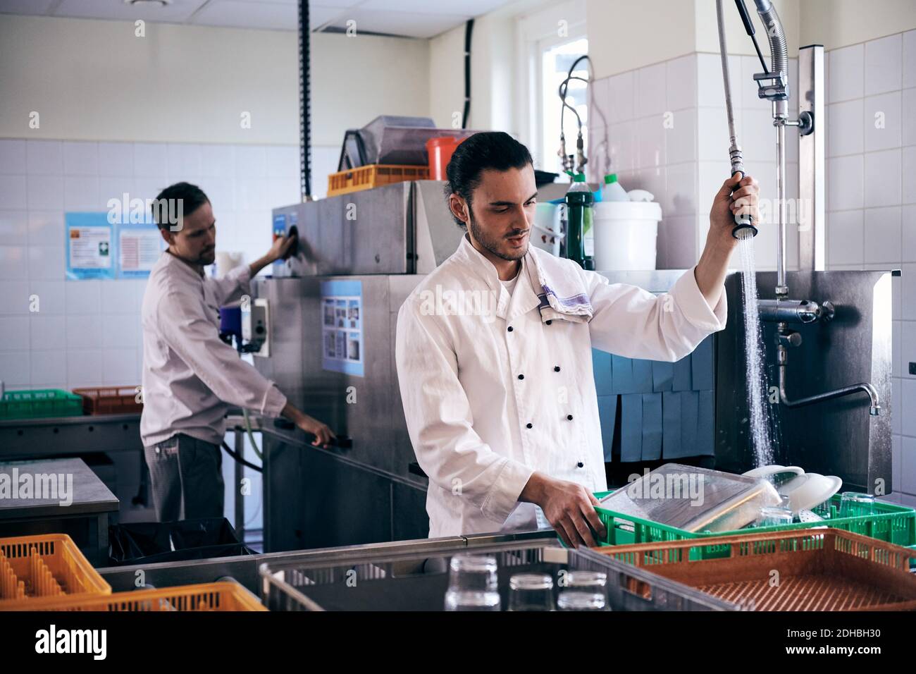 Chef spraying water on plates while colleague working in commercial ...