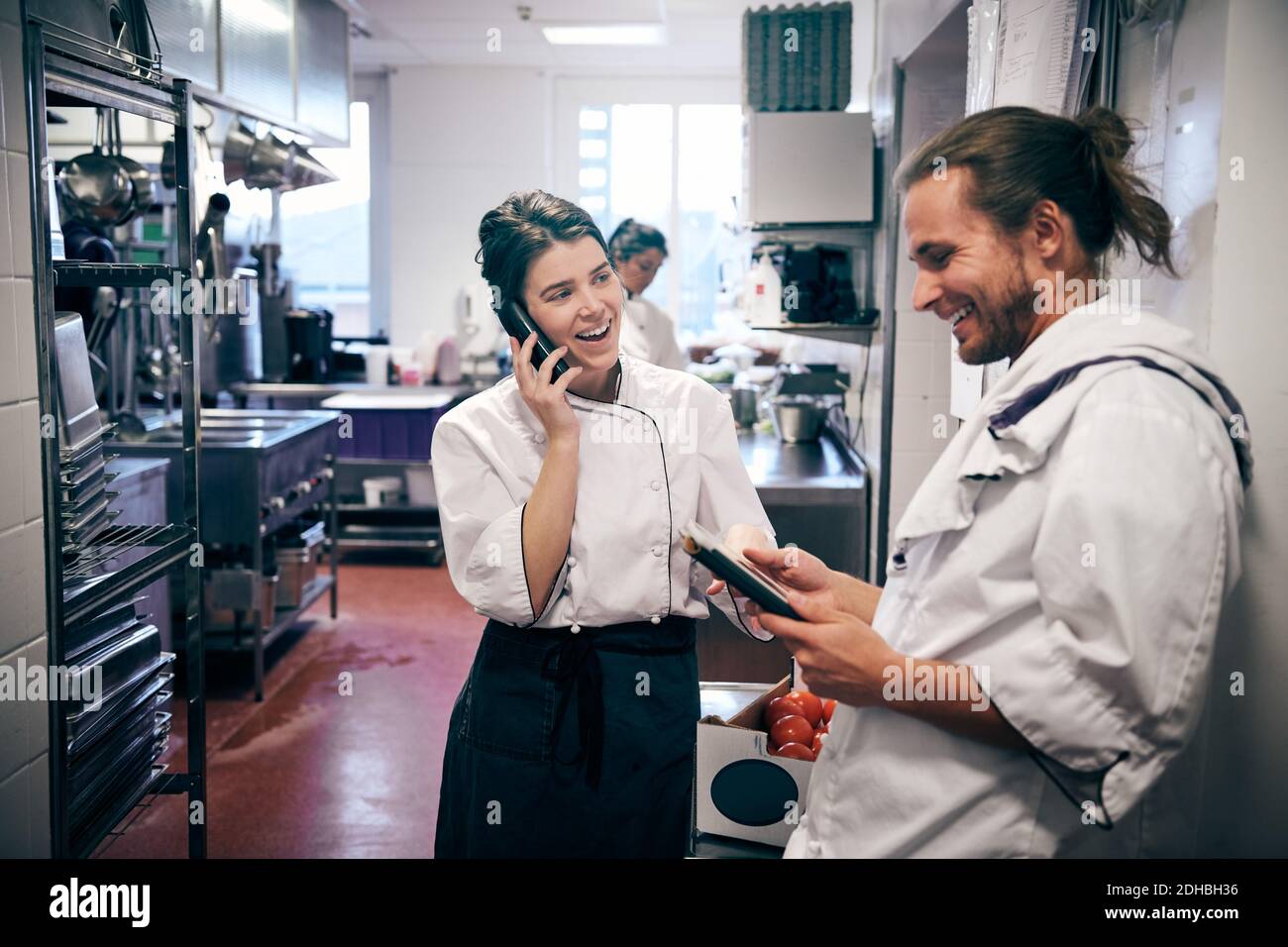 Male and female chefs using cordless phone and digital tablet in ...