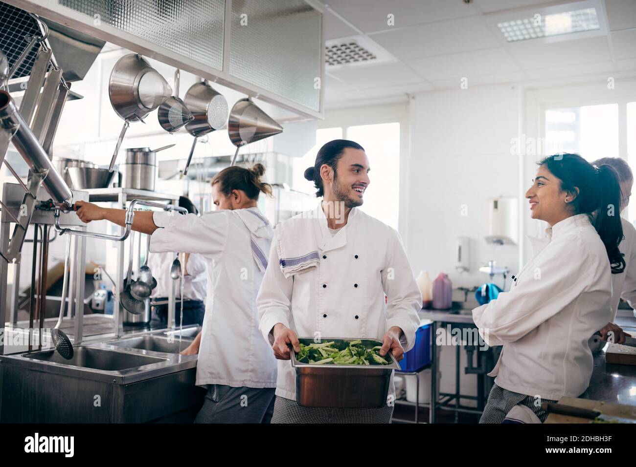 Male and female chefs communicating while preparing food in commercial ...