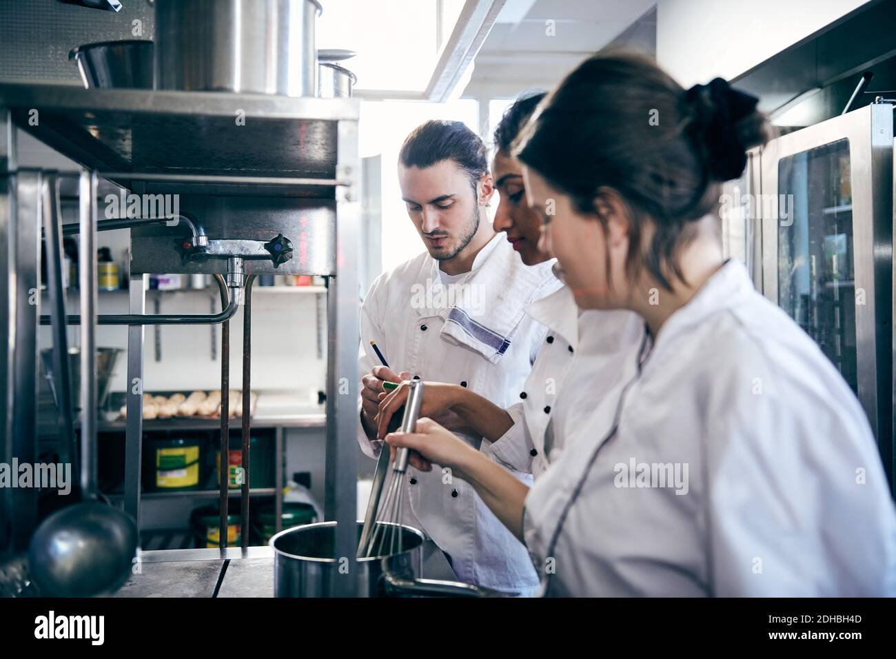 Female chefs cooking food while male colleague writing in notepad at ...