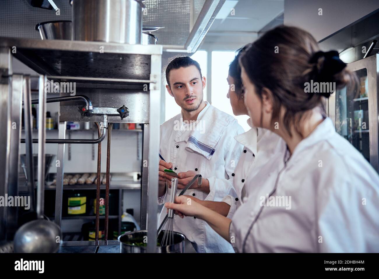 Male chef taking notes while looking at colleagues cooking in ...