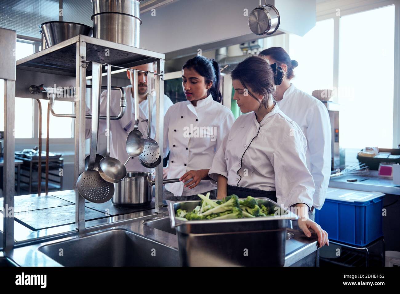 Chef team looking at colleague cooking food in commercial kitchen Stock ...