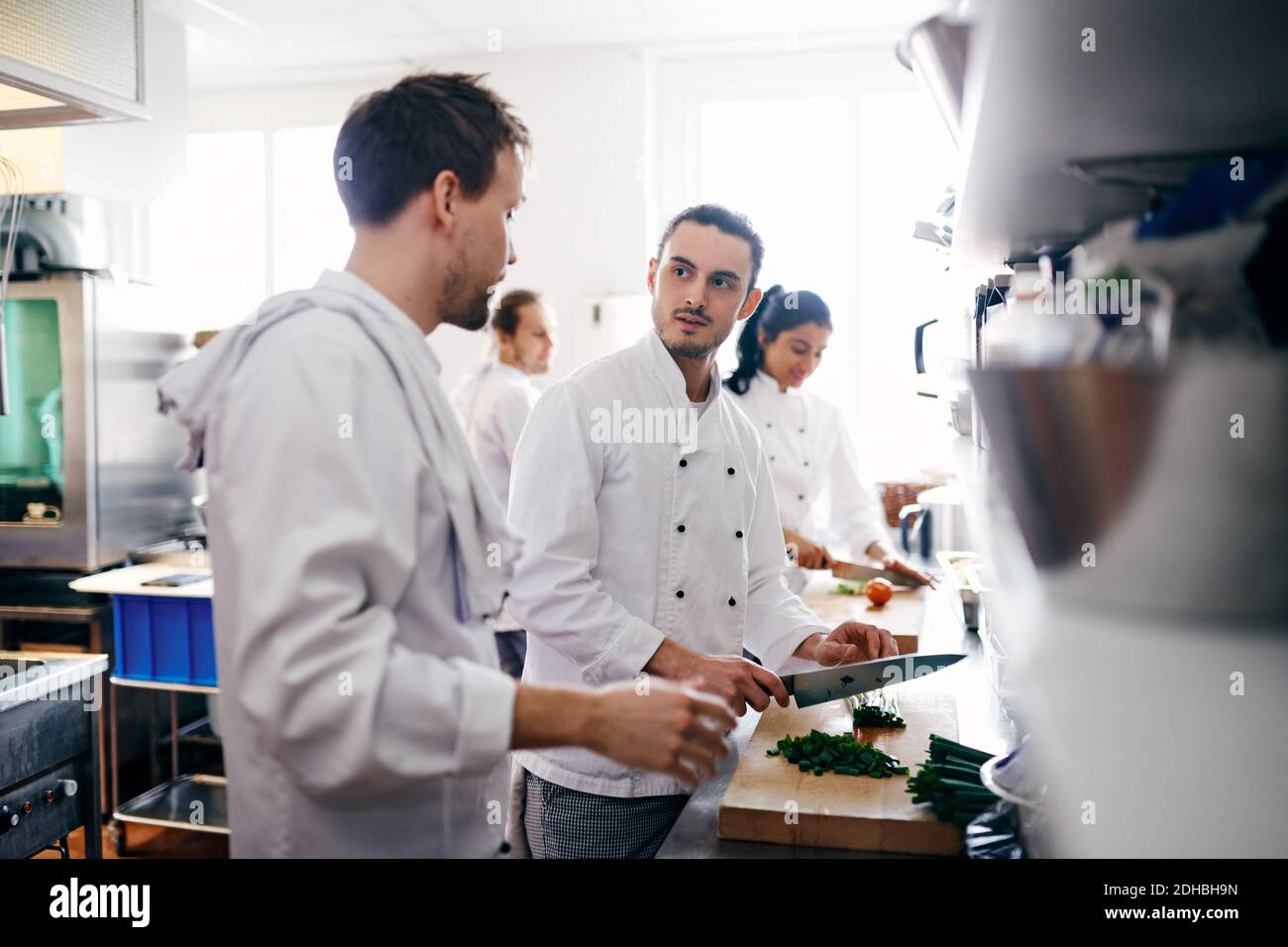Young chef talking with colleague while chopping vegetable in ...