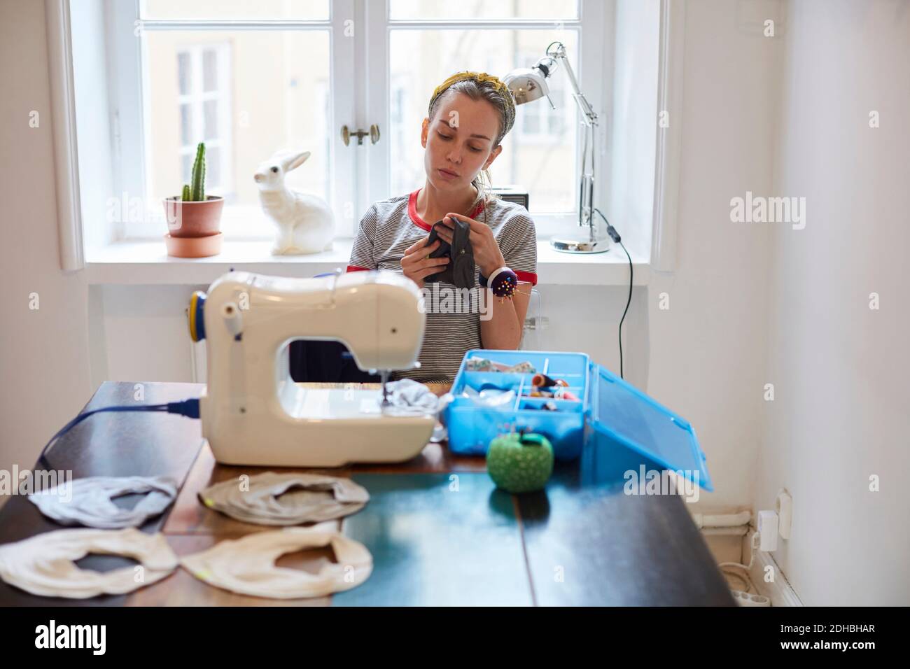 Tailor sewing scarf on machine while sitting against window at home ...