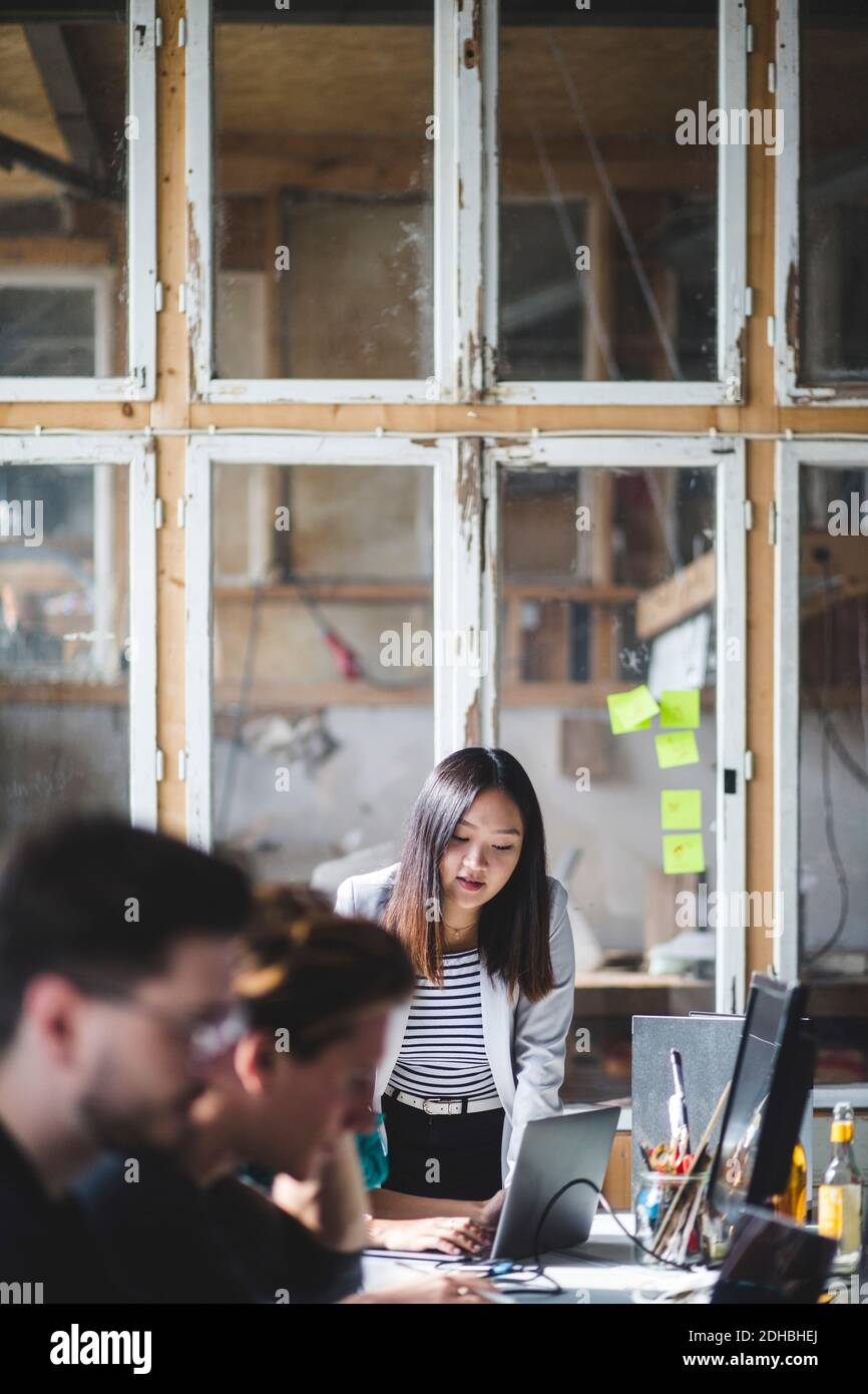 Confident female IT professional looking at colleague coding in laptop ...