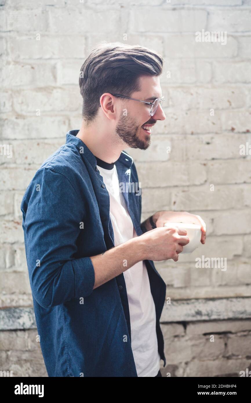 Side view of bearded smiling computer programmer holding coffee cup ...