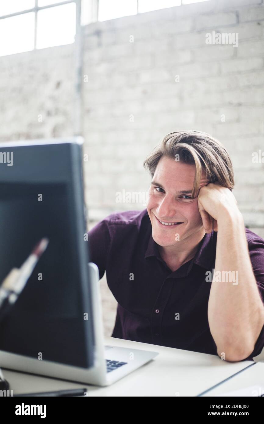 Portrait of smiling young male programmer coding at desk in office ...