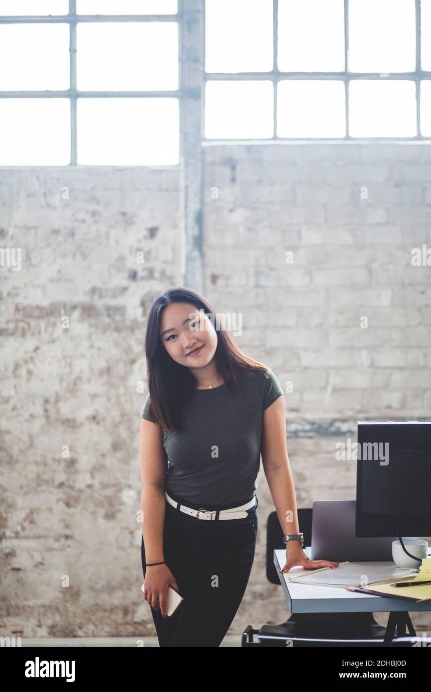 Portrait of confident female computer programmer standing beside desk ...