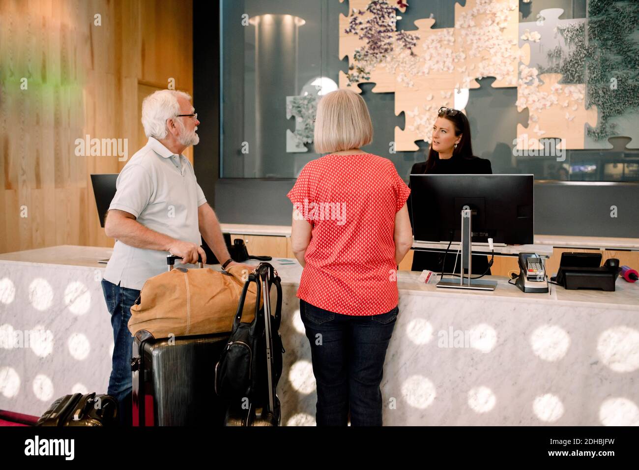 Senior couple talking to receptionist while standing at reception in ...