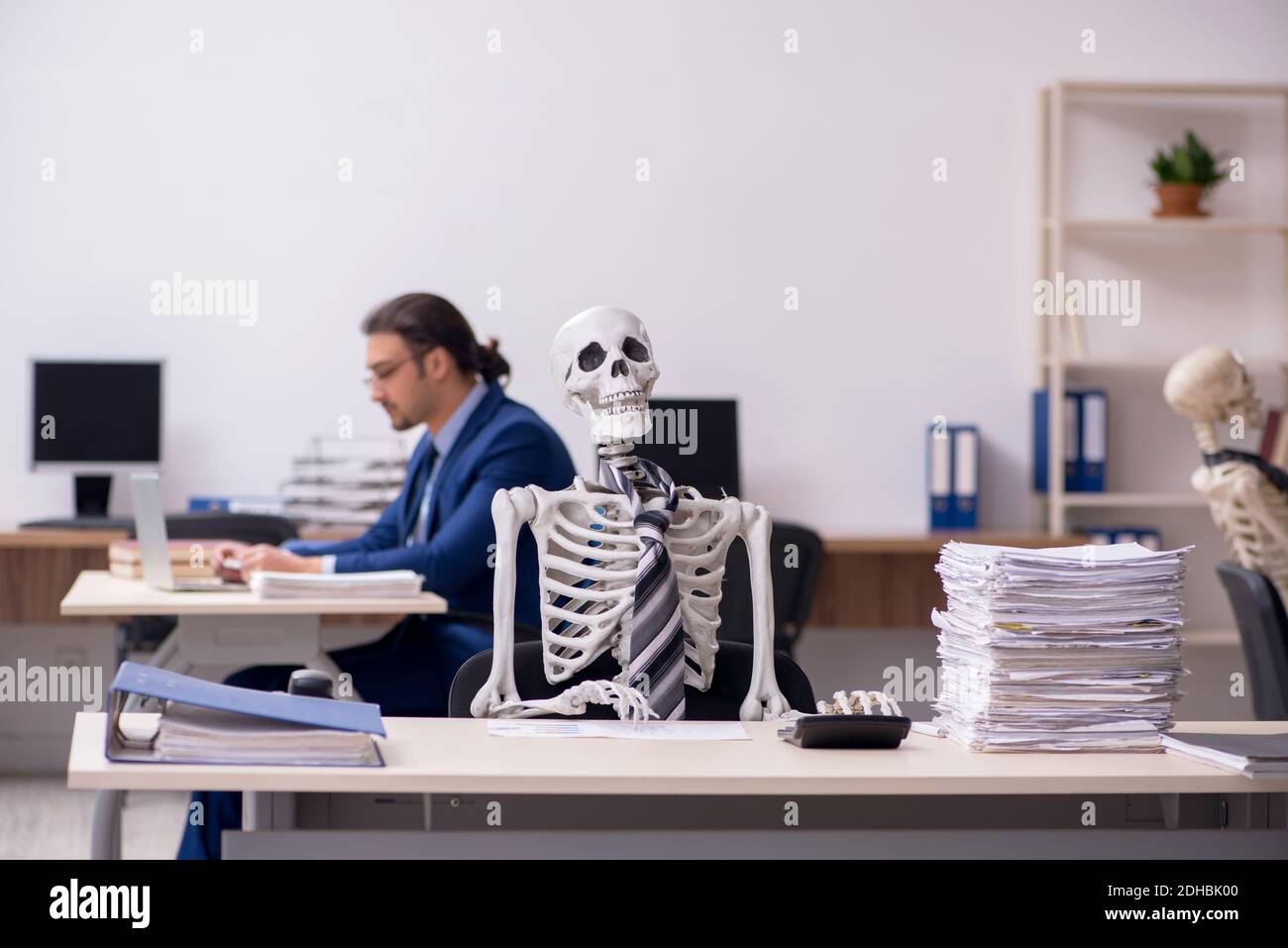 Young male employee with skeletons in the office Stock Photo - Alamy
