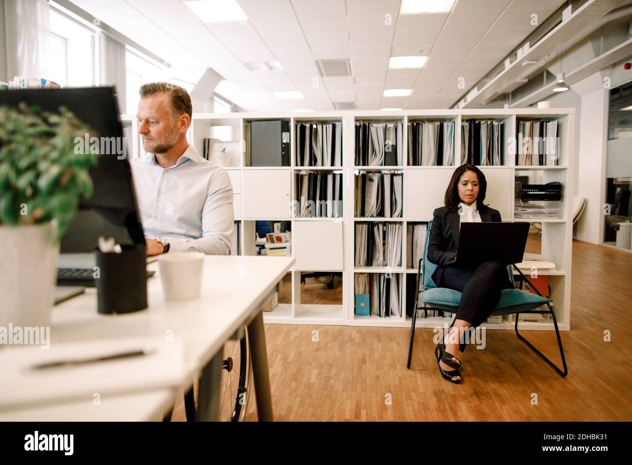 Serious businessman working at office desk while female colleague using ...