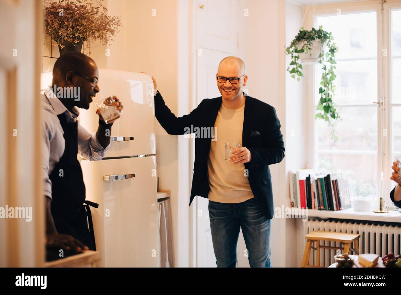 Smiling friends drinking water while standing by refrigerator in ...