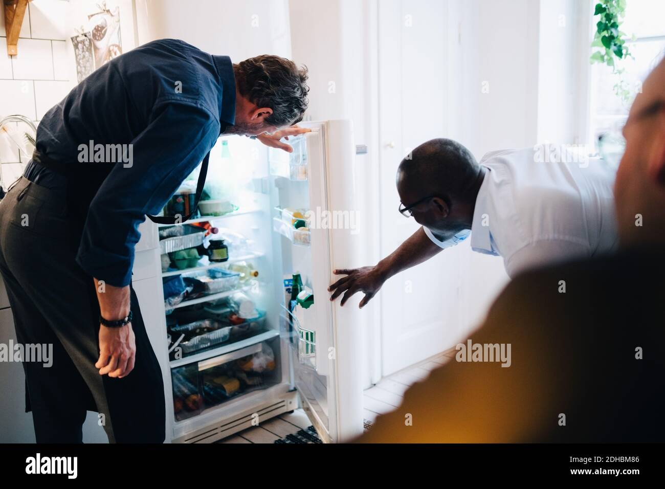 Mature male friends looking into refrigerator at kitchen Stock Photo ...