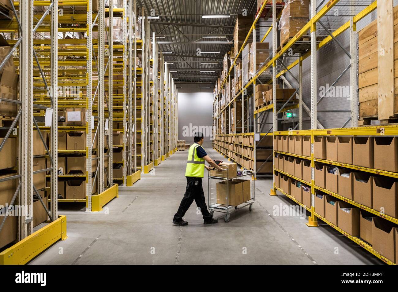 Full length of young warehouse worker pushing cart on aisle in ...
