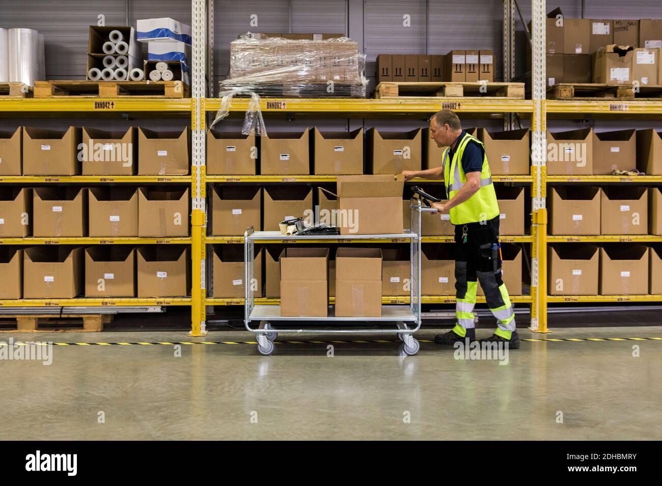 Full length side view of senior male worker pushing cart with cardboard ...