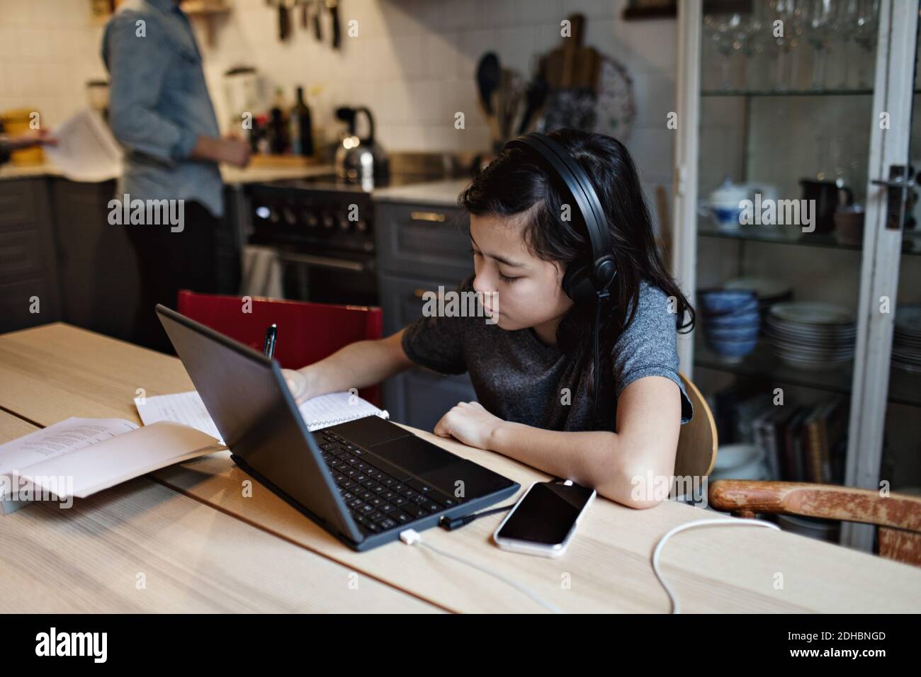 Serious boy doing homework while using laptop and mobile phone at home ...