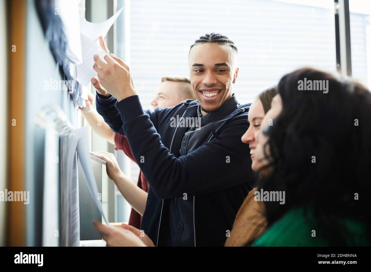 Happy young man with female friends checking papers on bulletin board ...