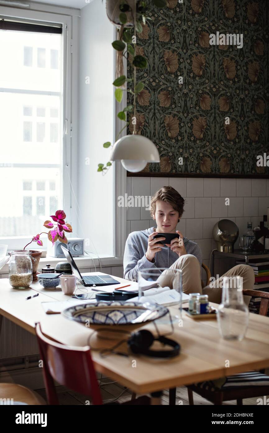 Teenage boy using mobile phone while studying at home Stock Photo - Alamy