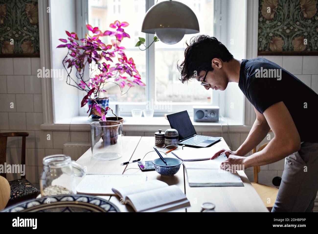 Side view of dedicated young man reading book on table while studying ...