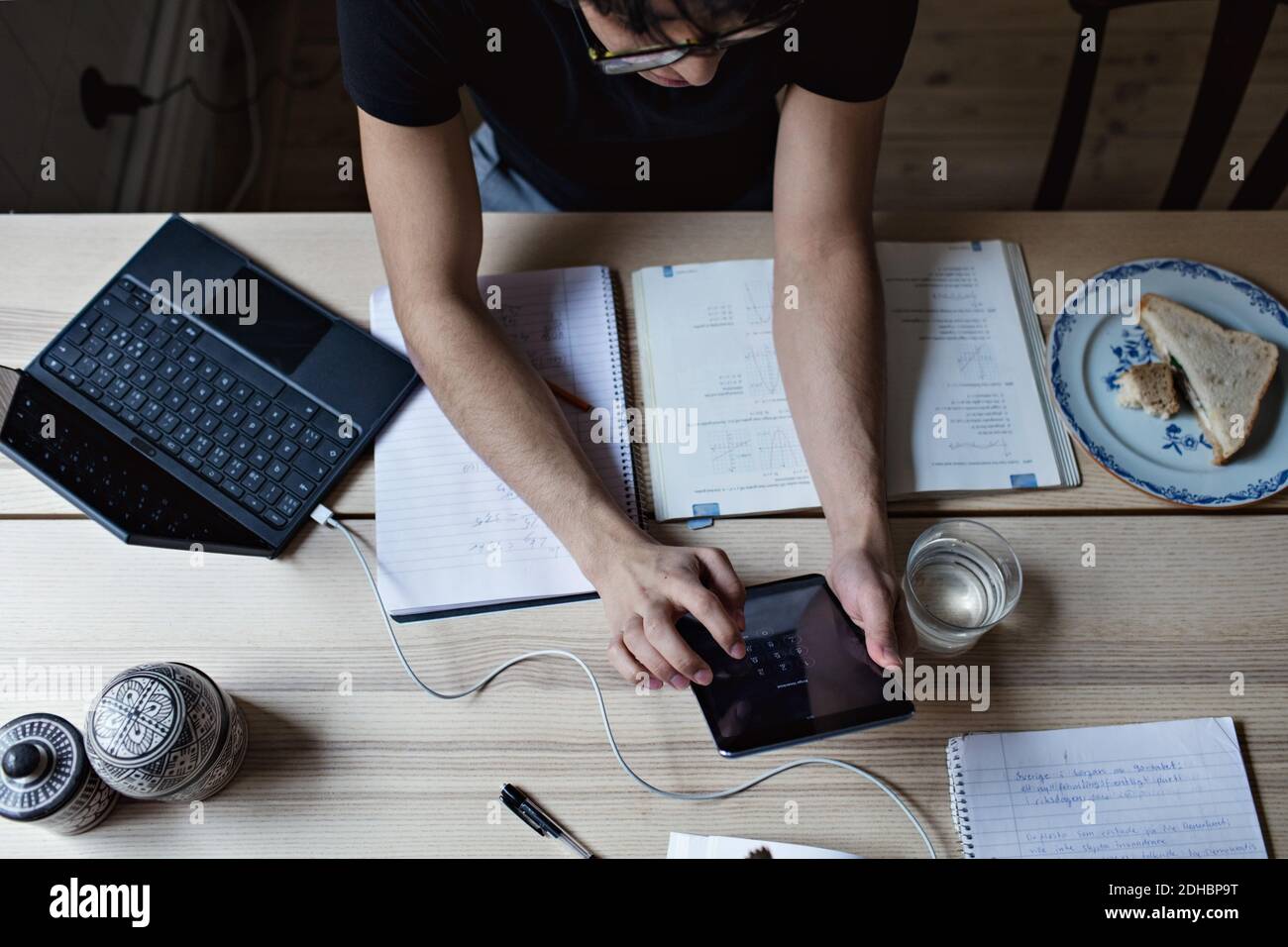 High angle view of studious young man using digital tablet while doing ...