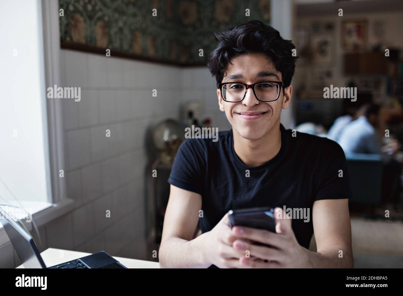 Portrait of smiling young man using social media on mobile phone while ...