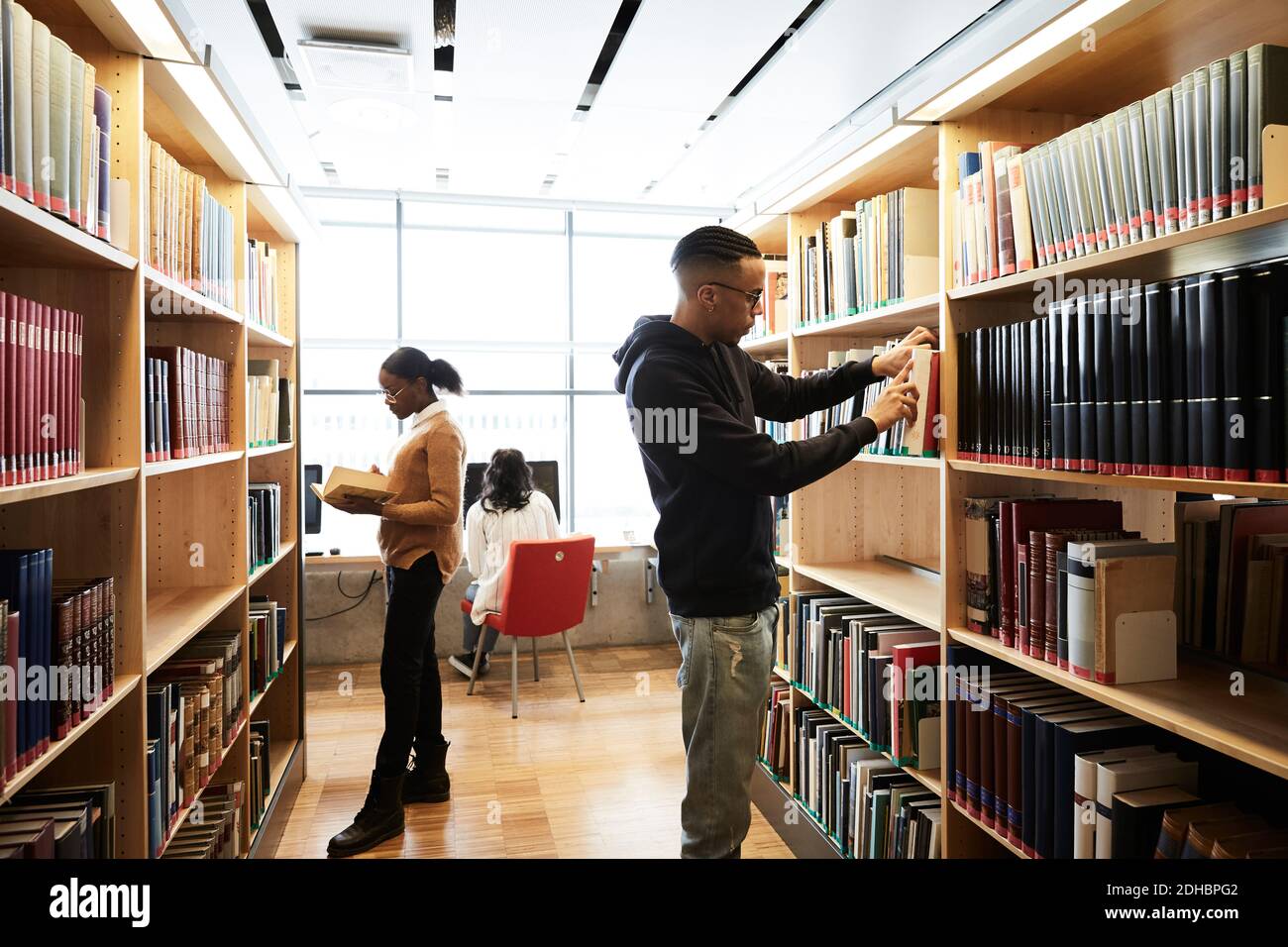 Students searching book while woman using computer in library at ...