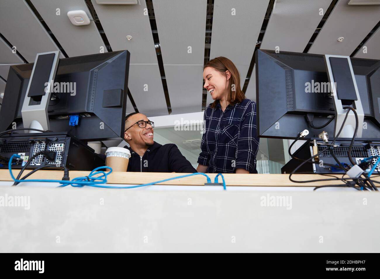 Low angle view of smiling friends talking while using computers at ...