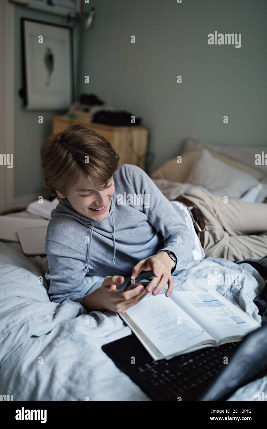 Smiling teenage boy using social media on mobile phone while doing ...