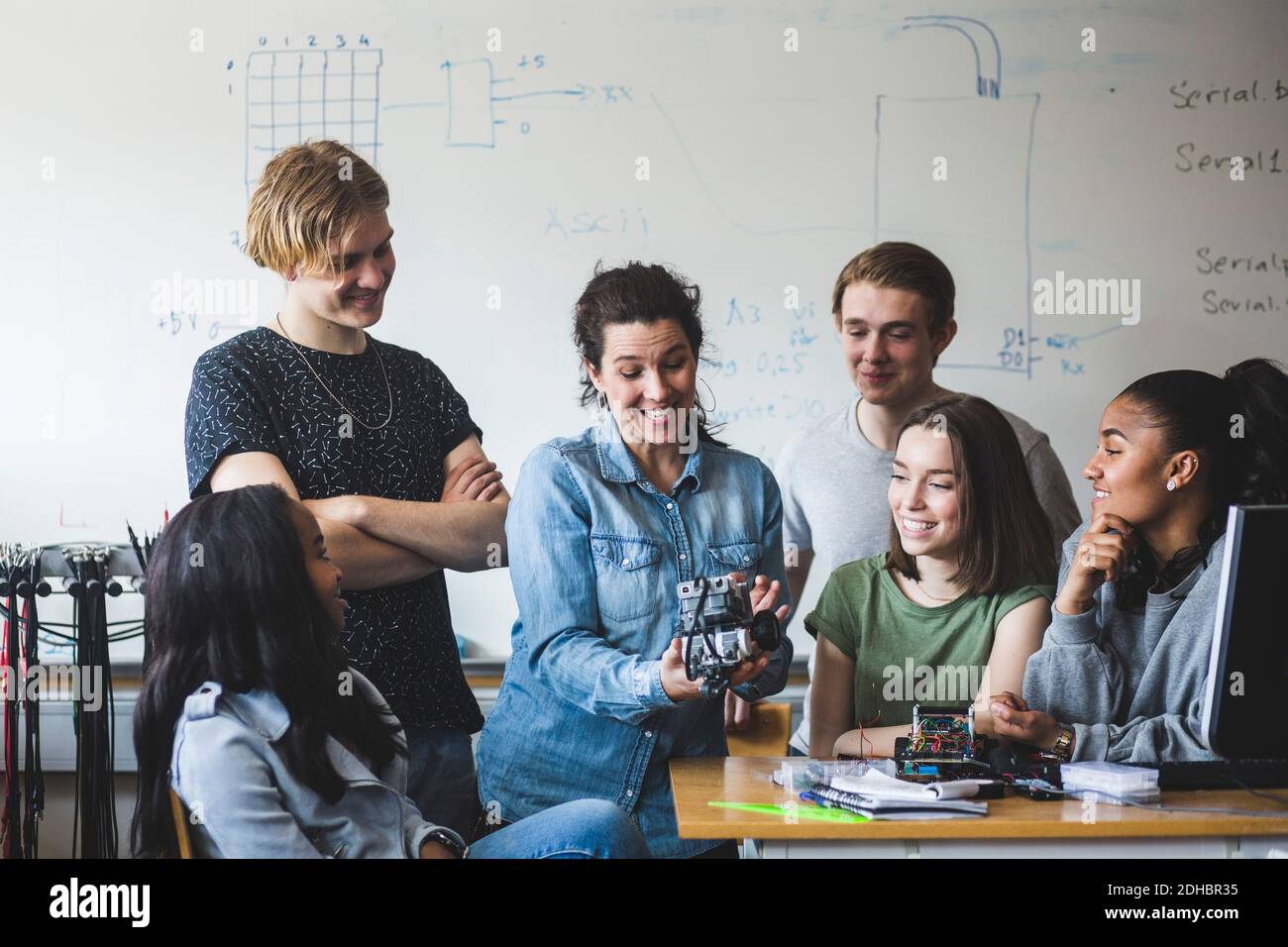 Surprised teacher examining robot while sitting amidst students against ...