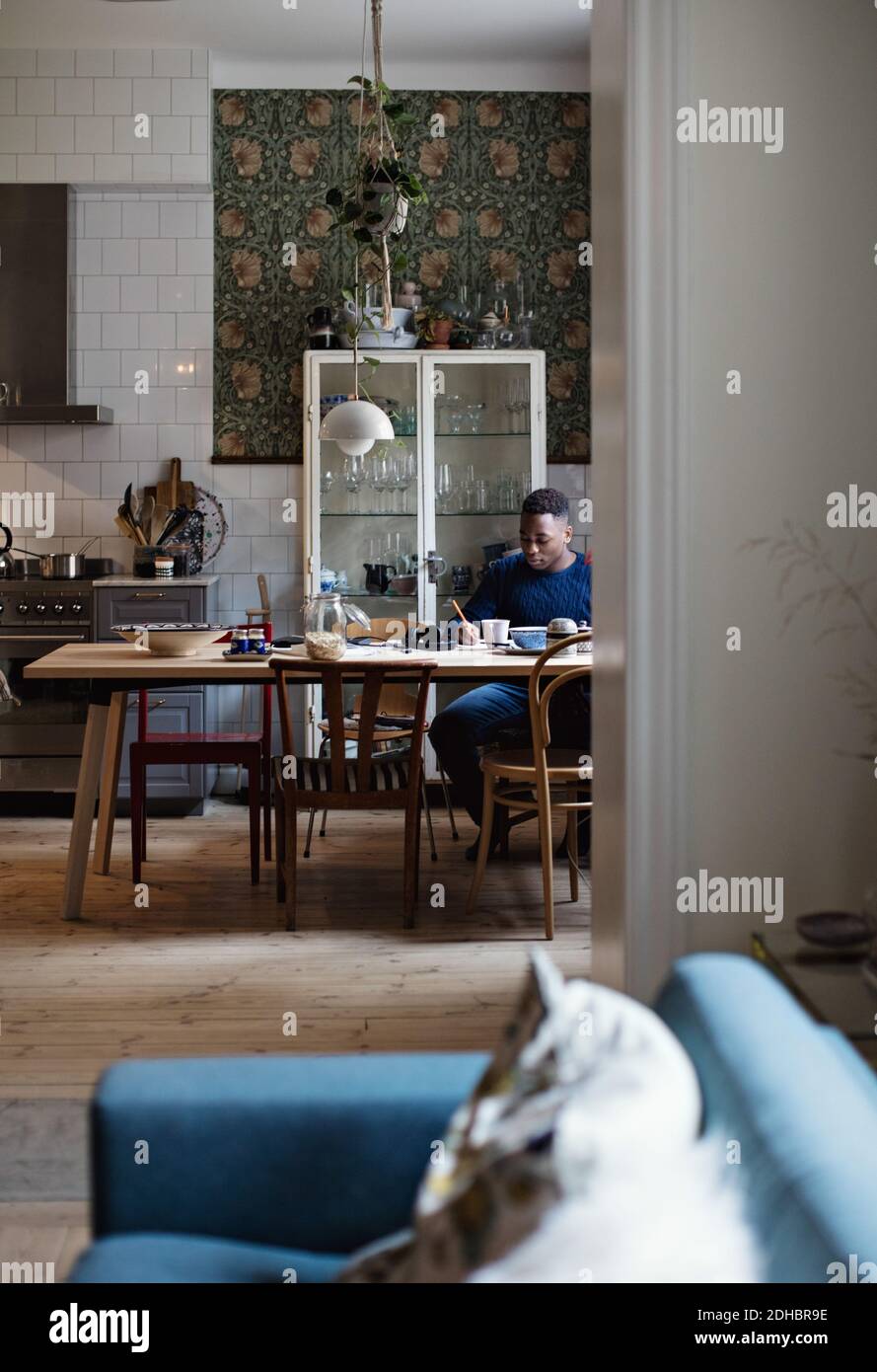 Full length of teenage boy doing homework while sitting at dining table ...