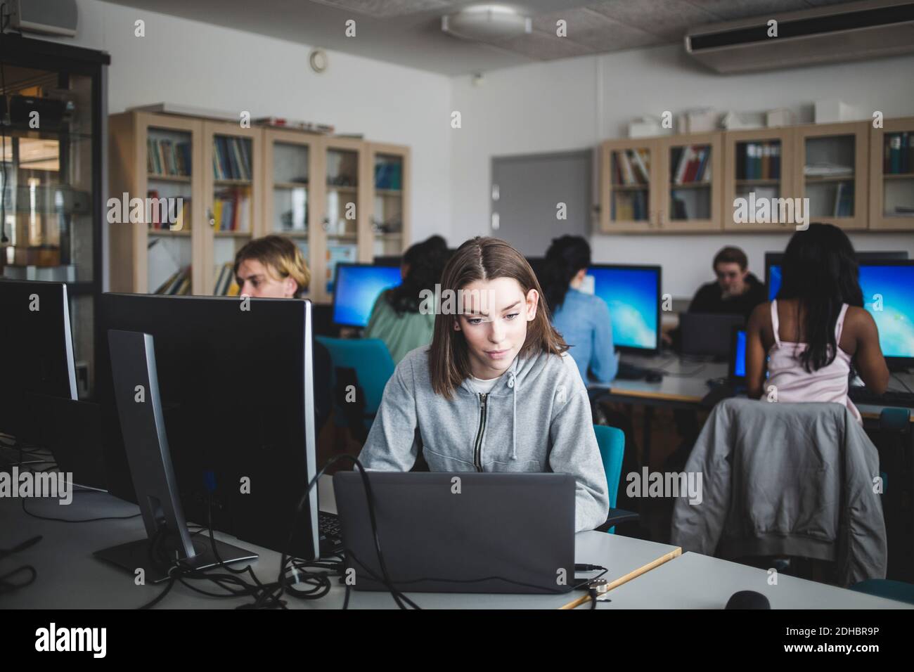 Confident female high school student using laptop at desk against ...