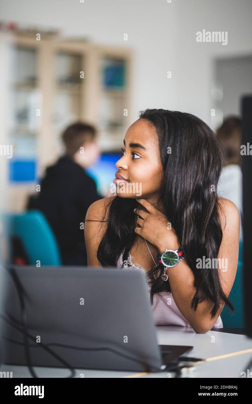 Confident female high school student looking away while sitting with ...
